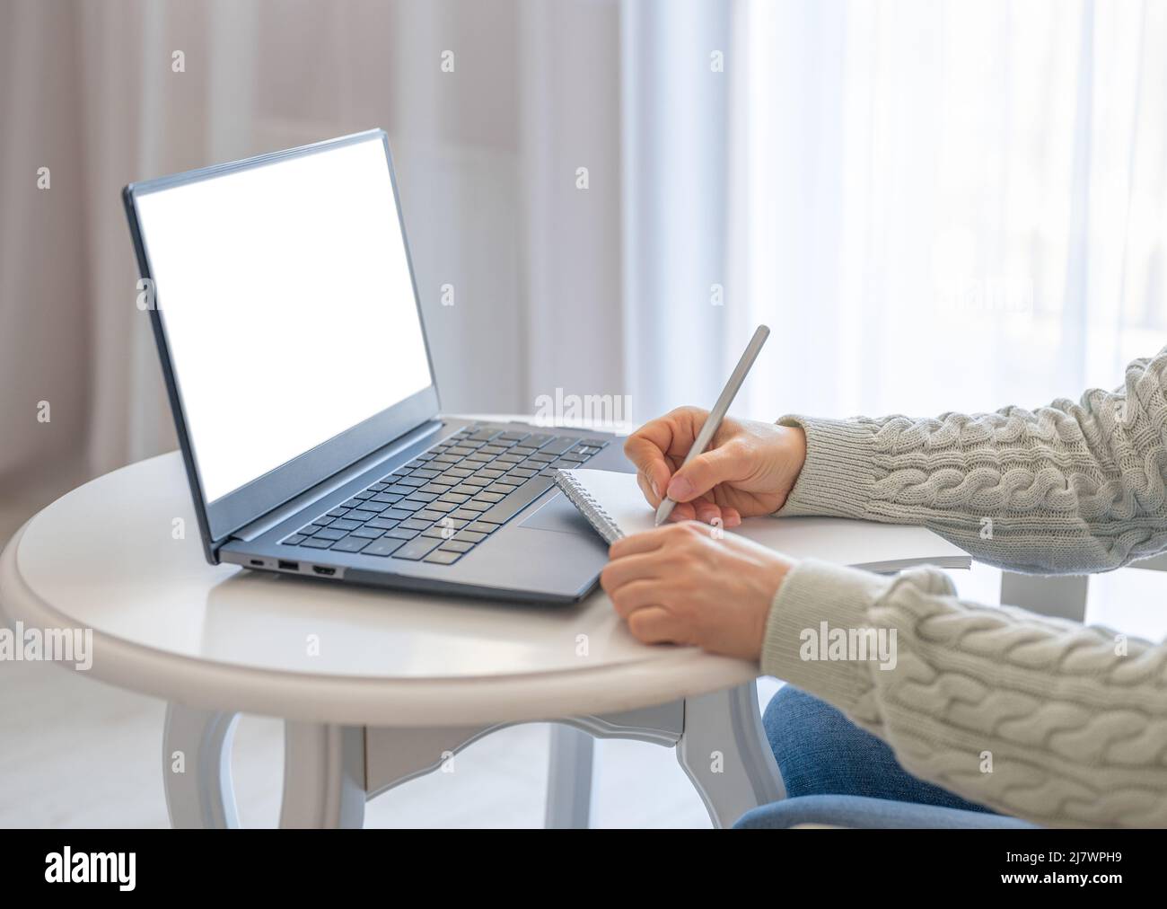 woman taking notes in notebook while using mockup laptop with blank ...
