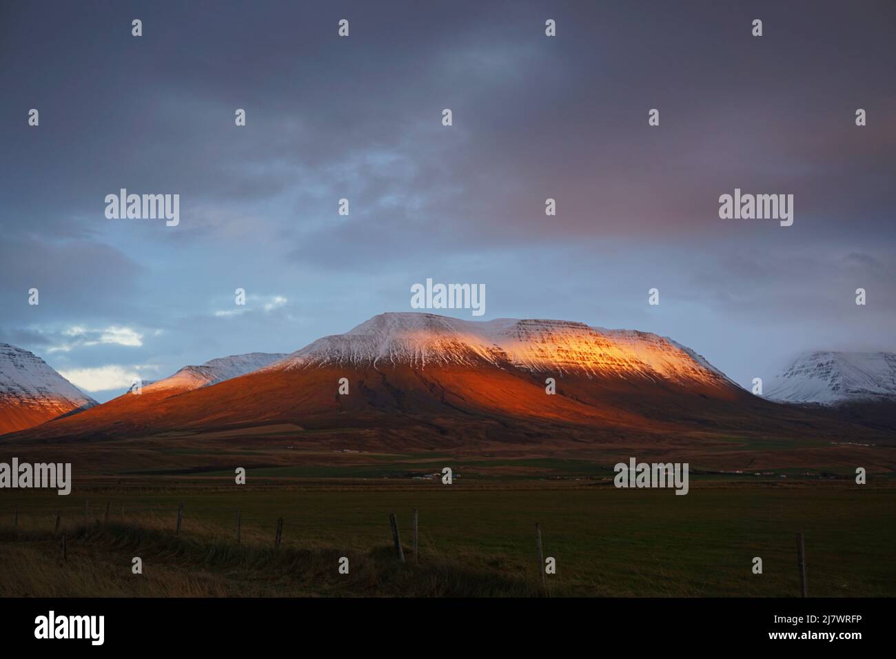 Snowy mountains with plain field and grey sky during golden hour near ...