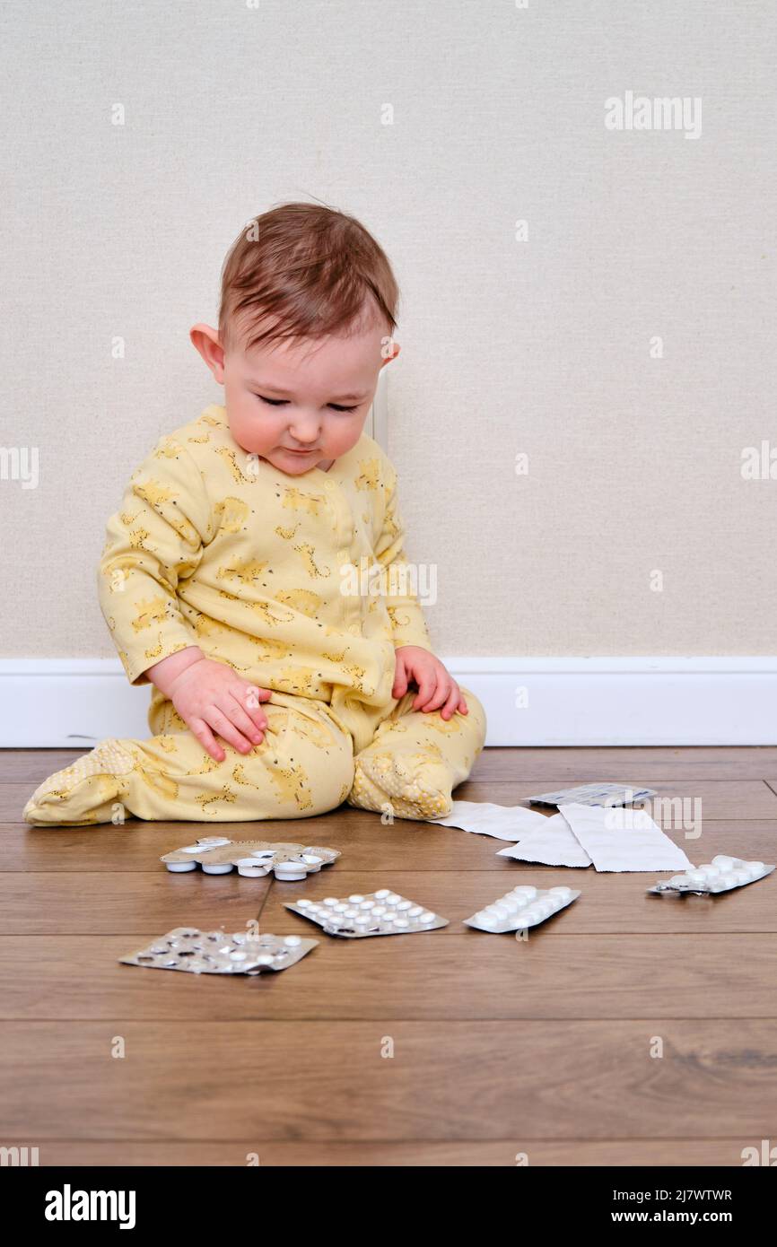 Toddler baby boy plays with medicines in a package while sitting on the ...