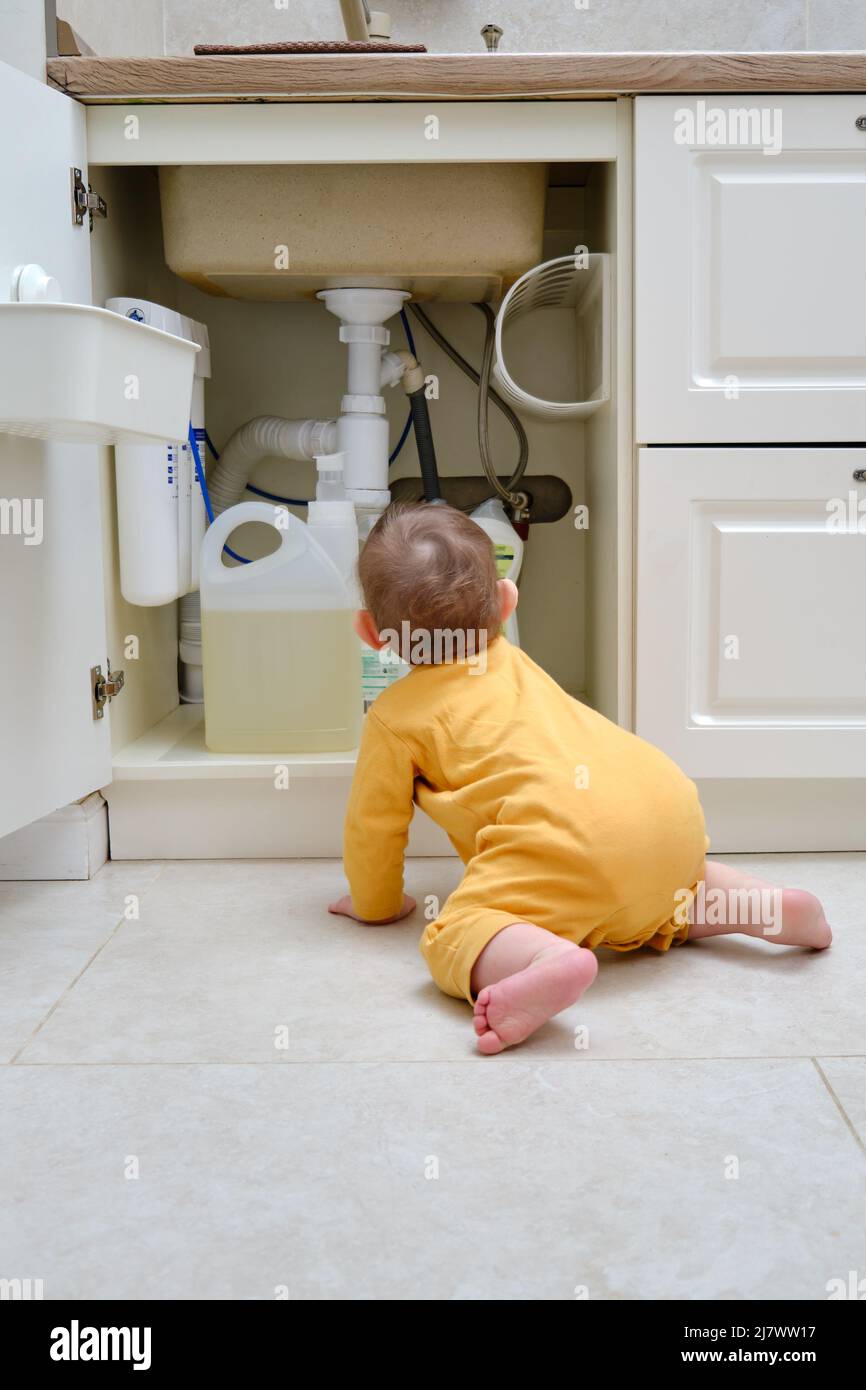 Toddler baby boy is playing with detergents and cleaning products in an ...