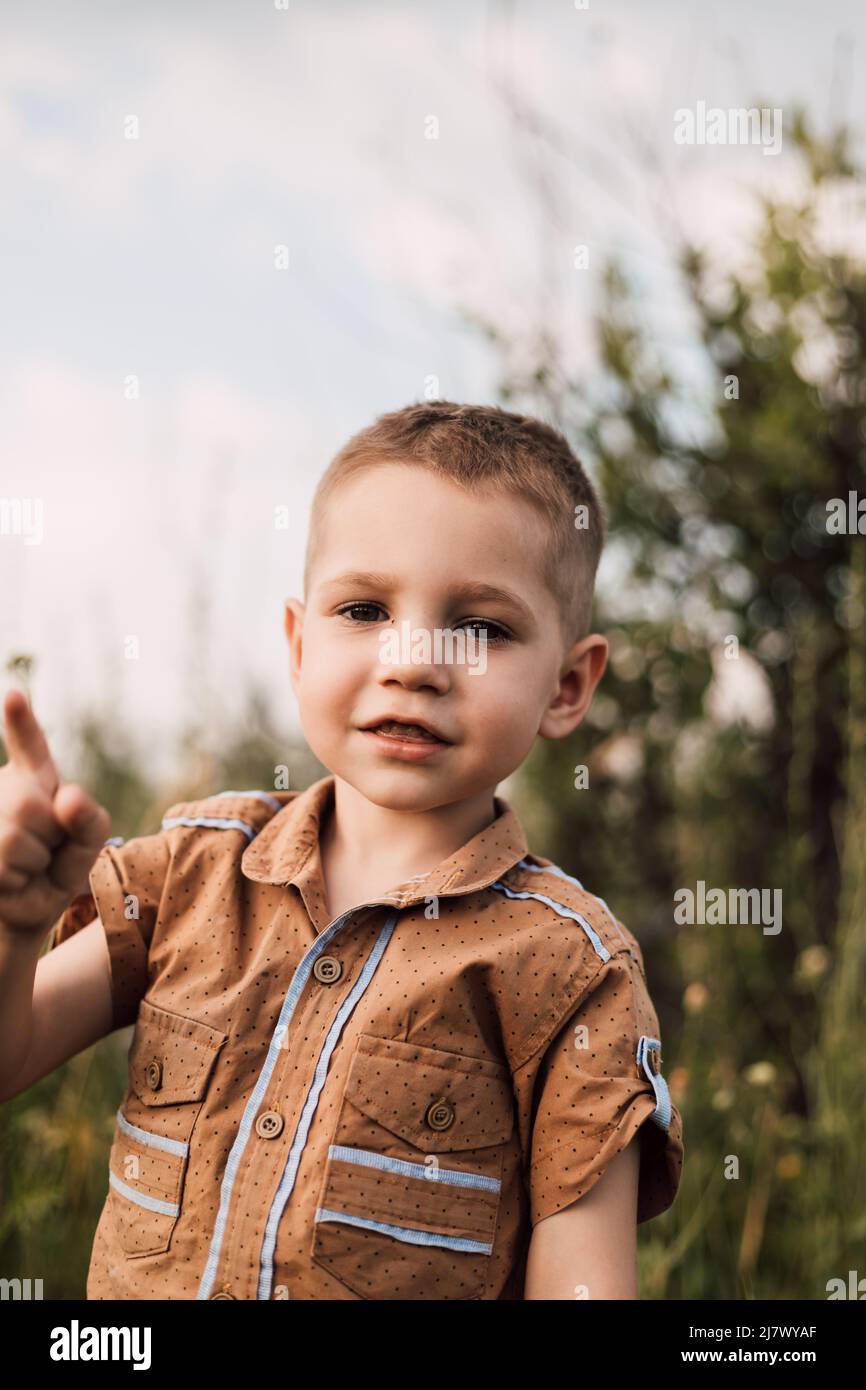 A little boy stands in a village in a field, smiling and raising his ...