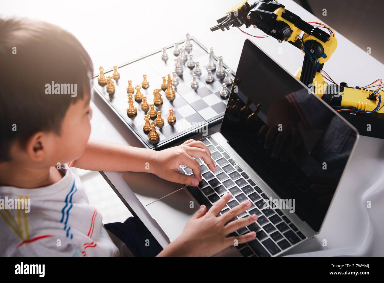 Asian little boy programming code to robot machine arm on laptop for ...