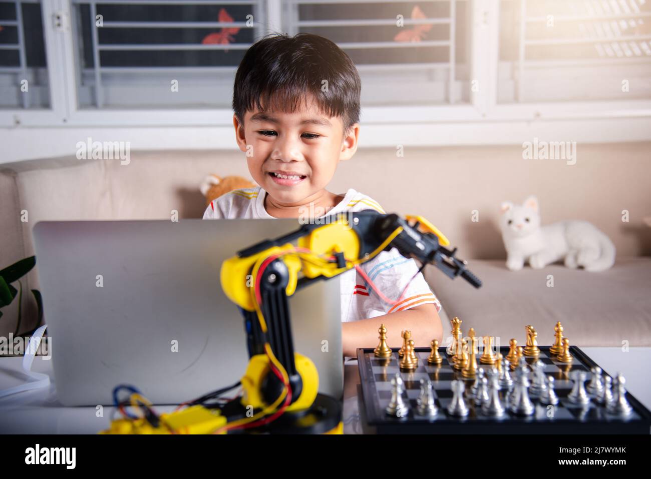 Asian little boy programming code to robot machine arm on laptop for ...