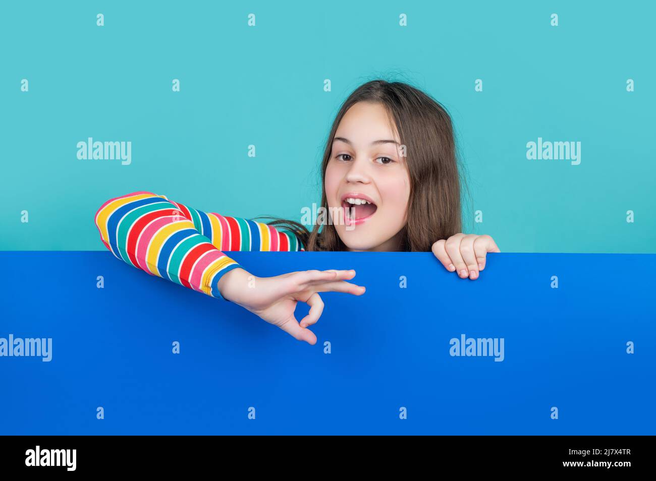 amazed kid behind blank blue paper with copy space for advertisement ...