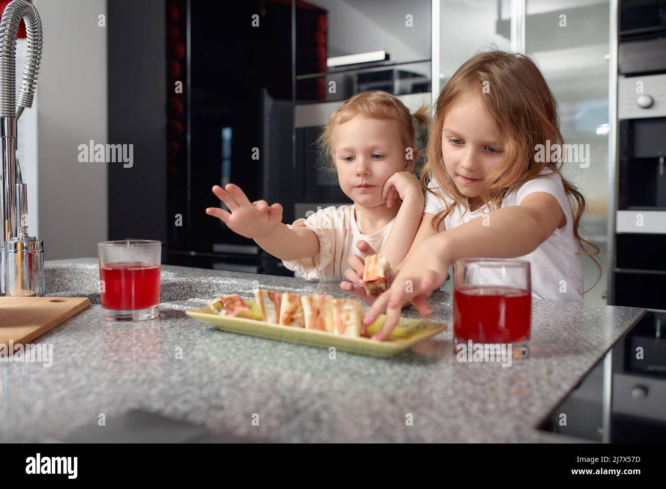 Two little girls siblings having fun and eating on the kitchen at home ...