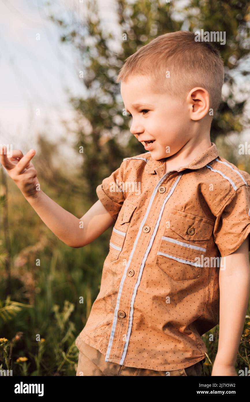 A little boy stands in a village in a field, smiling and raising his ...