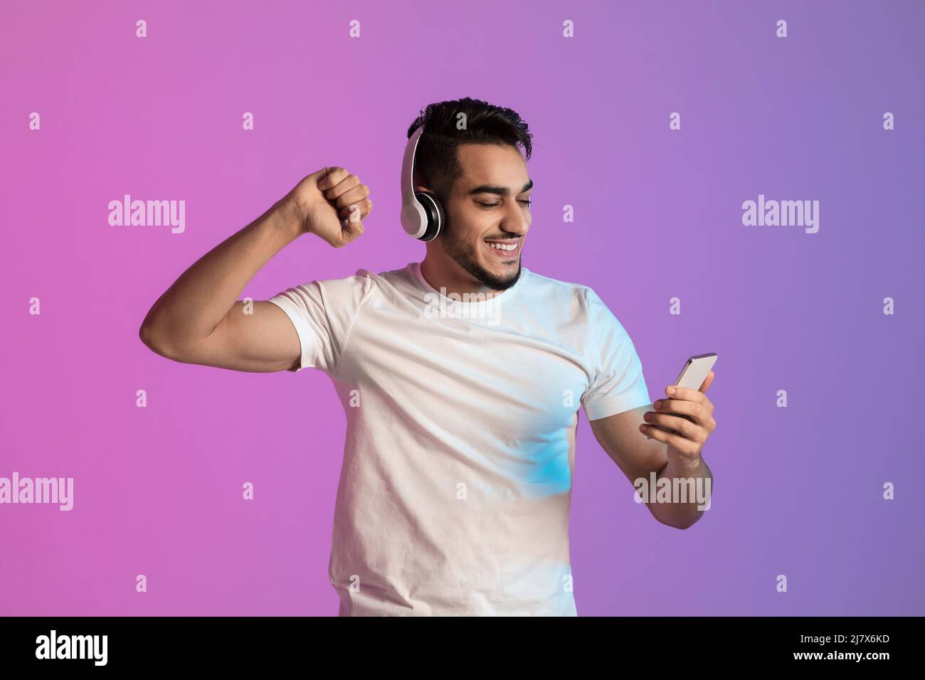 Happy young Arab man dancing to music in headphones, looking at ...