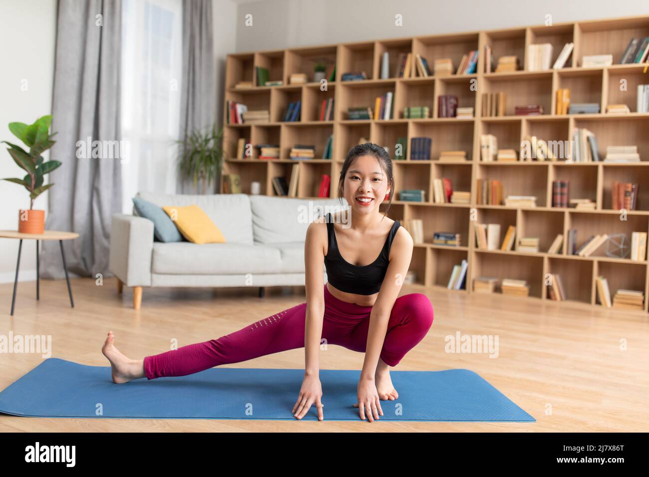 Home workout. Young asian lady stretching legs on yoga mat in living ...