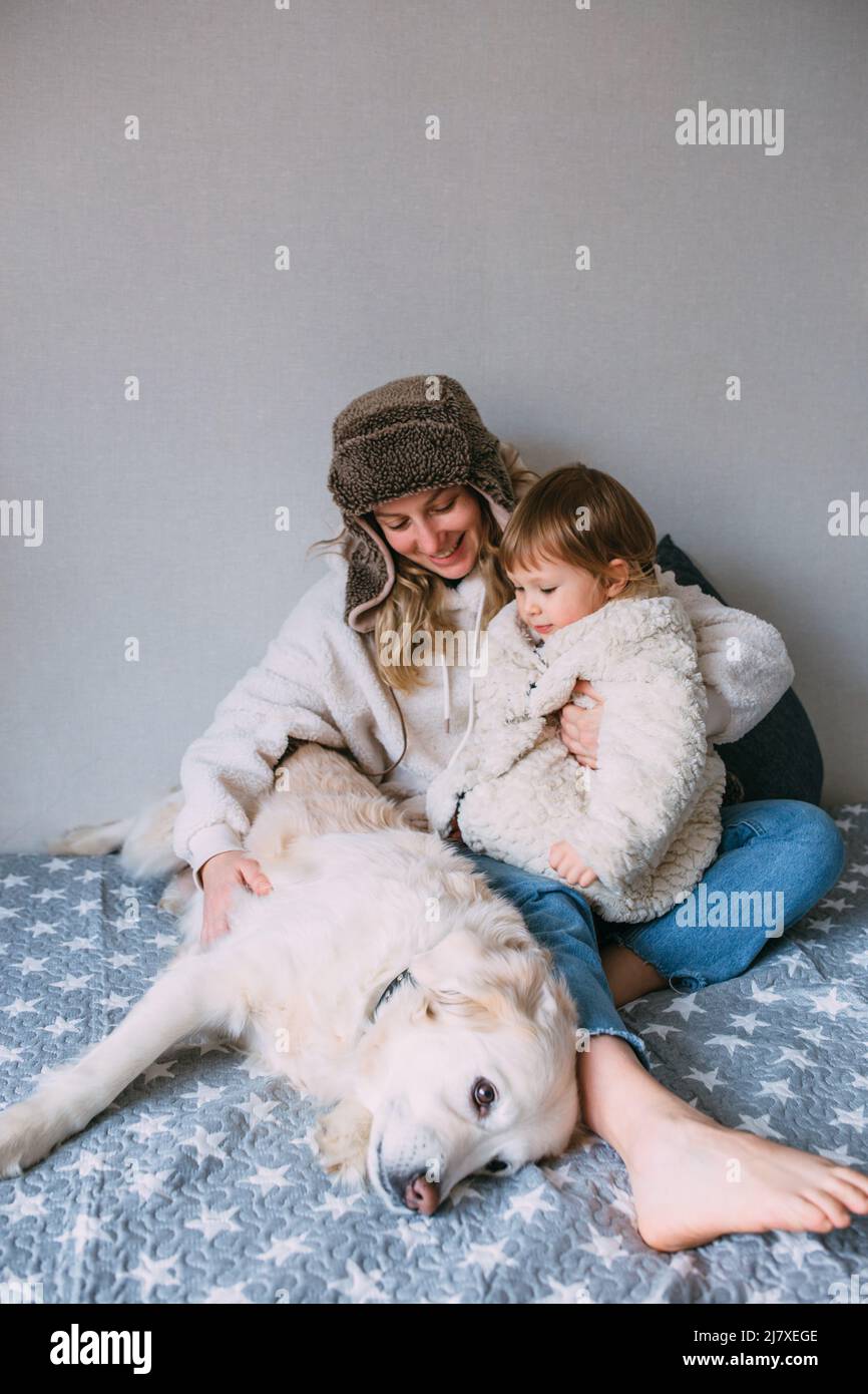 Mom and daughter comfortably cuddle at home with their pet Labrador ...
