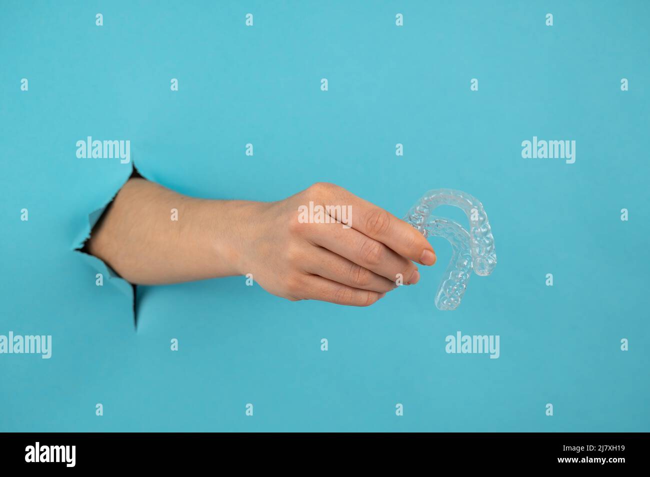 A female hand sticking out of a hole from a blue background holds ...