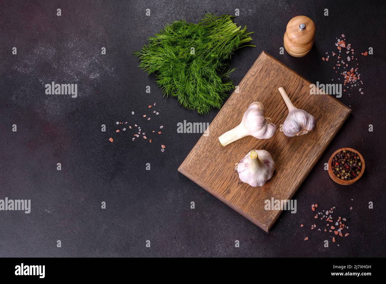 Heads of fresh white garlic on a wooden cutting board against a dark ...