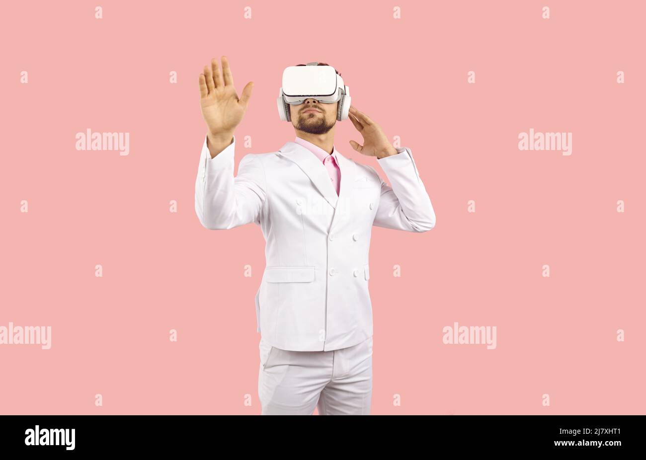 Young man standing on pink background experiencing virtual reality in ...