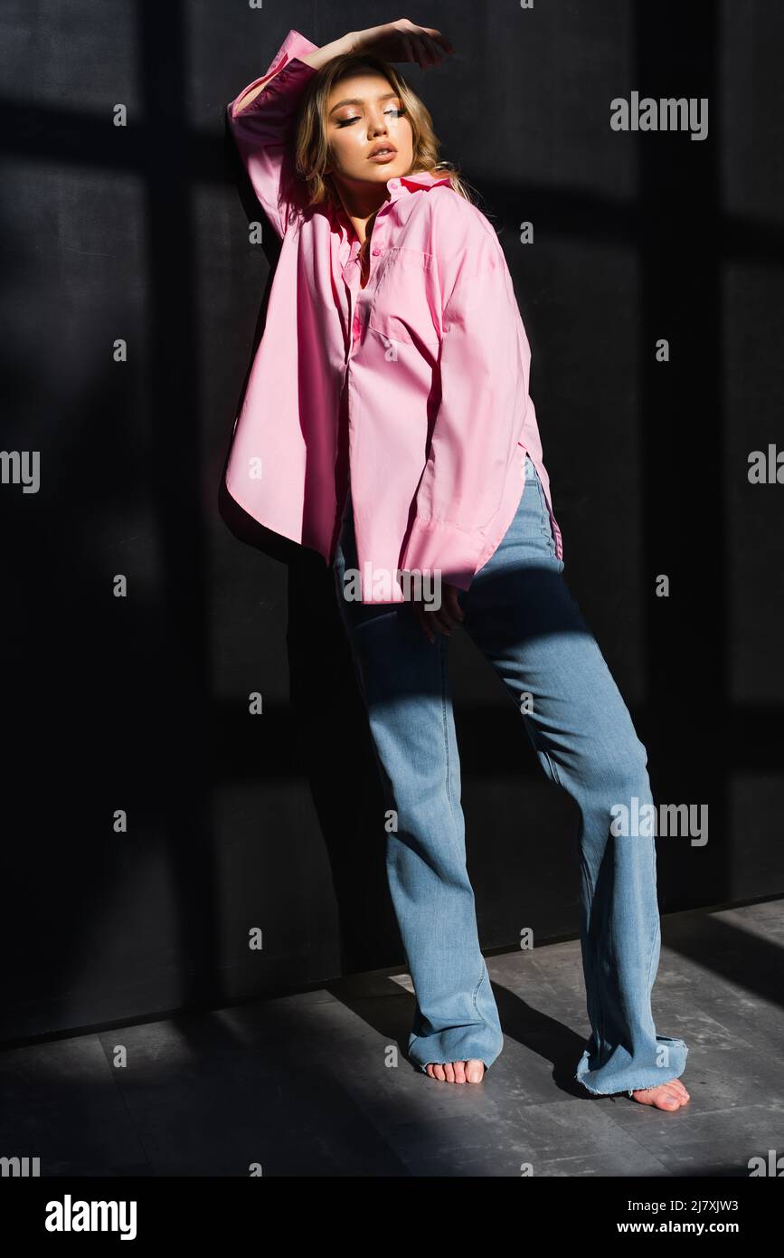 full length view of trendy barefoot woman posing with hand above head ...