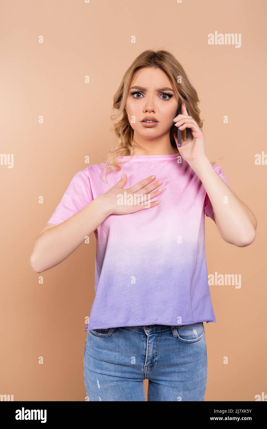 worried woman talking on mobile phone and touching chest isolated on ...