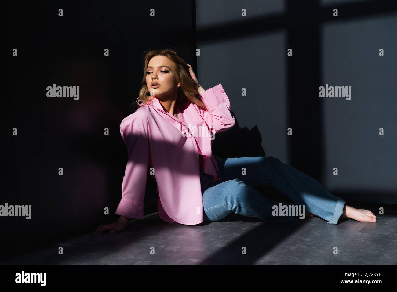 full length of barefoot woman in pink shirt sitting on floor near black ...