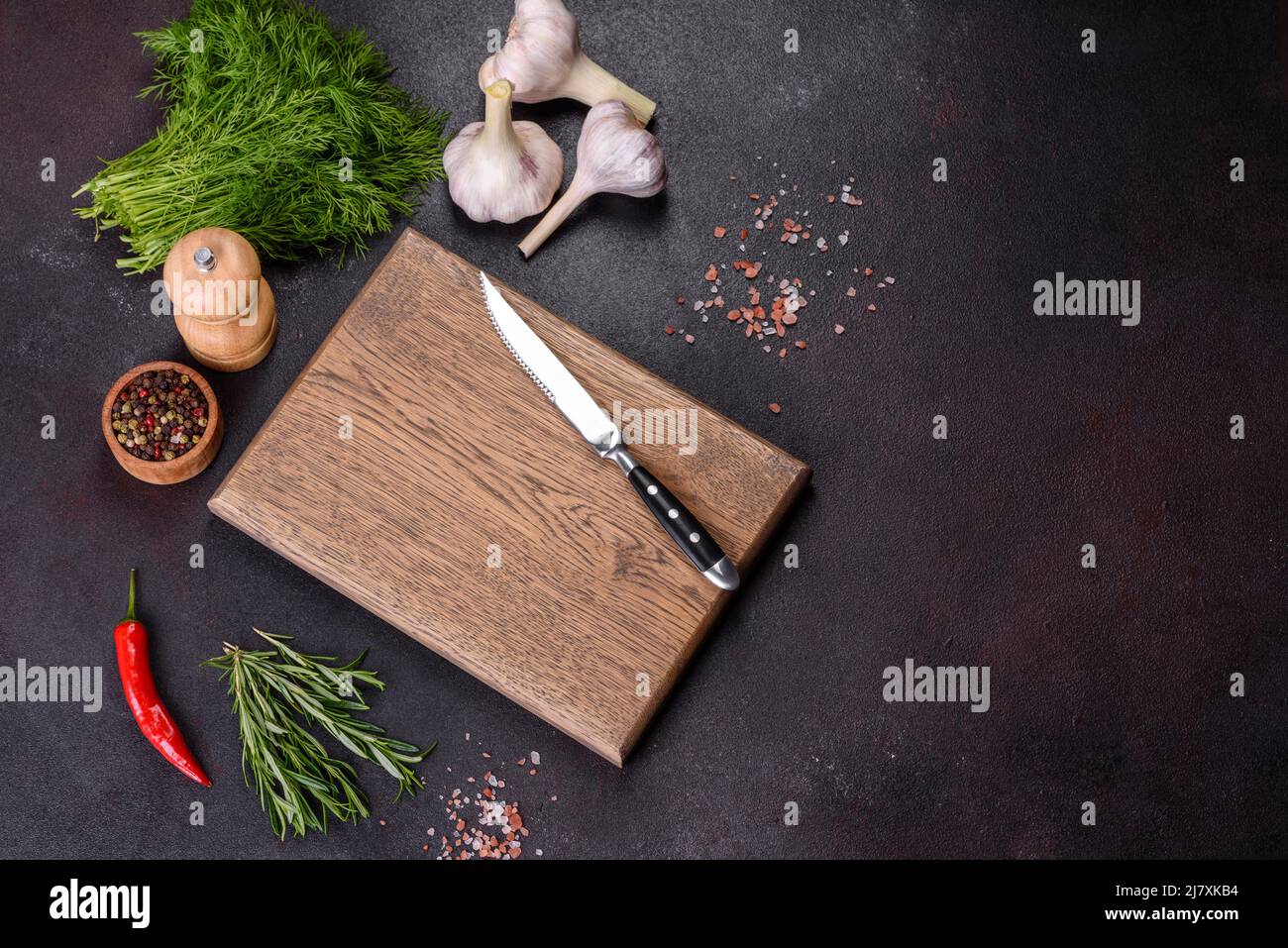 A wooden cutting board with spices, herbs, cherry tomatoes and salt on ...