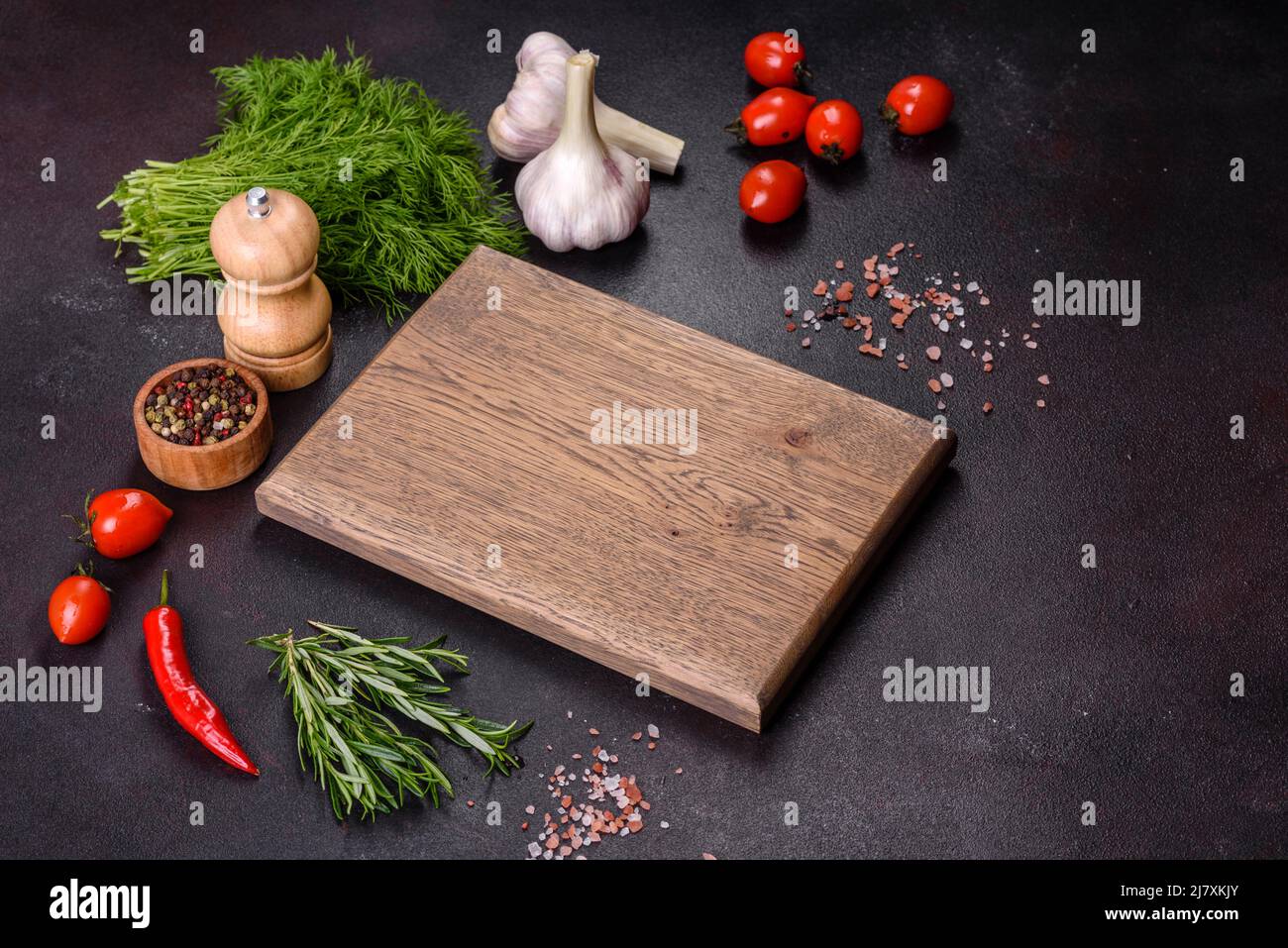 A wooden cutting board with spices, herbs, cherry tomatoes and salt on ...