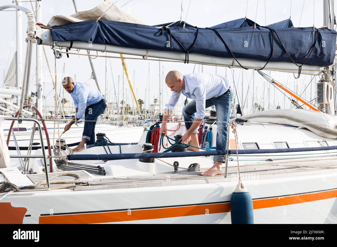 Two young men in blue shirts tidy up private sailing yacht in the ...