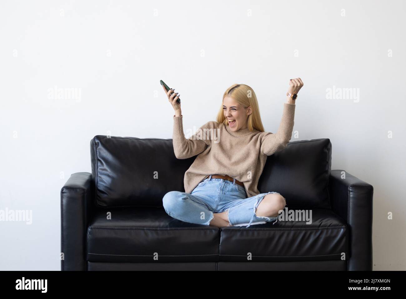 Excited woman celebrating success holding mobile phone sitting on a ...