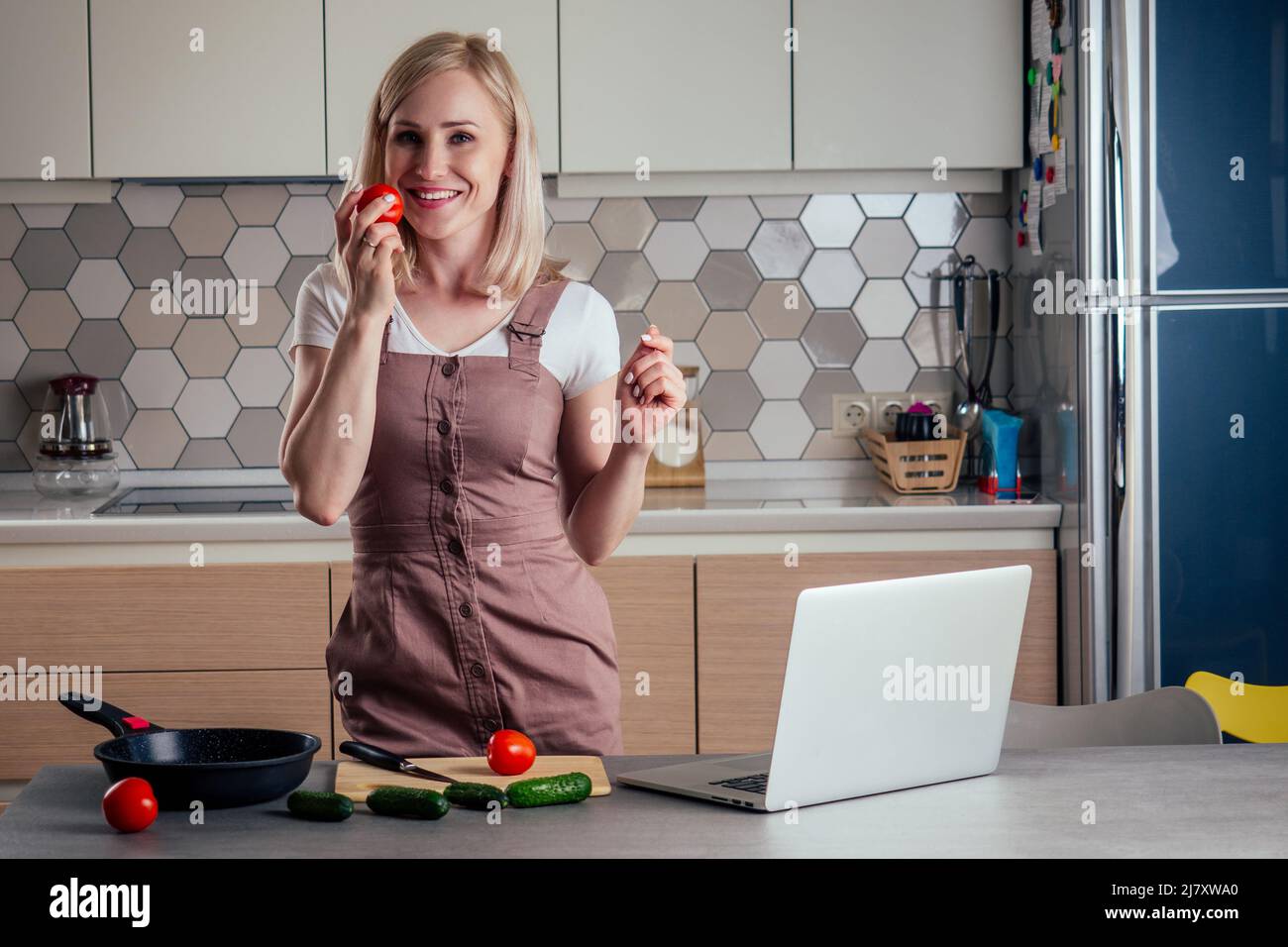 A beautiful blonde woman using laptop computer in the kitchen and cut ...