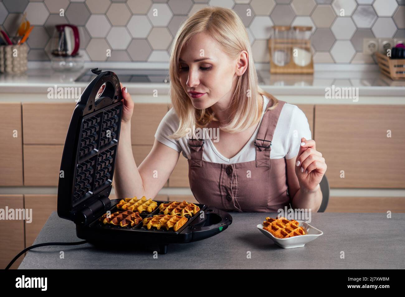 Woman taking fresh wafers out of waffle iron in kitchen Belgian waffles ...