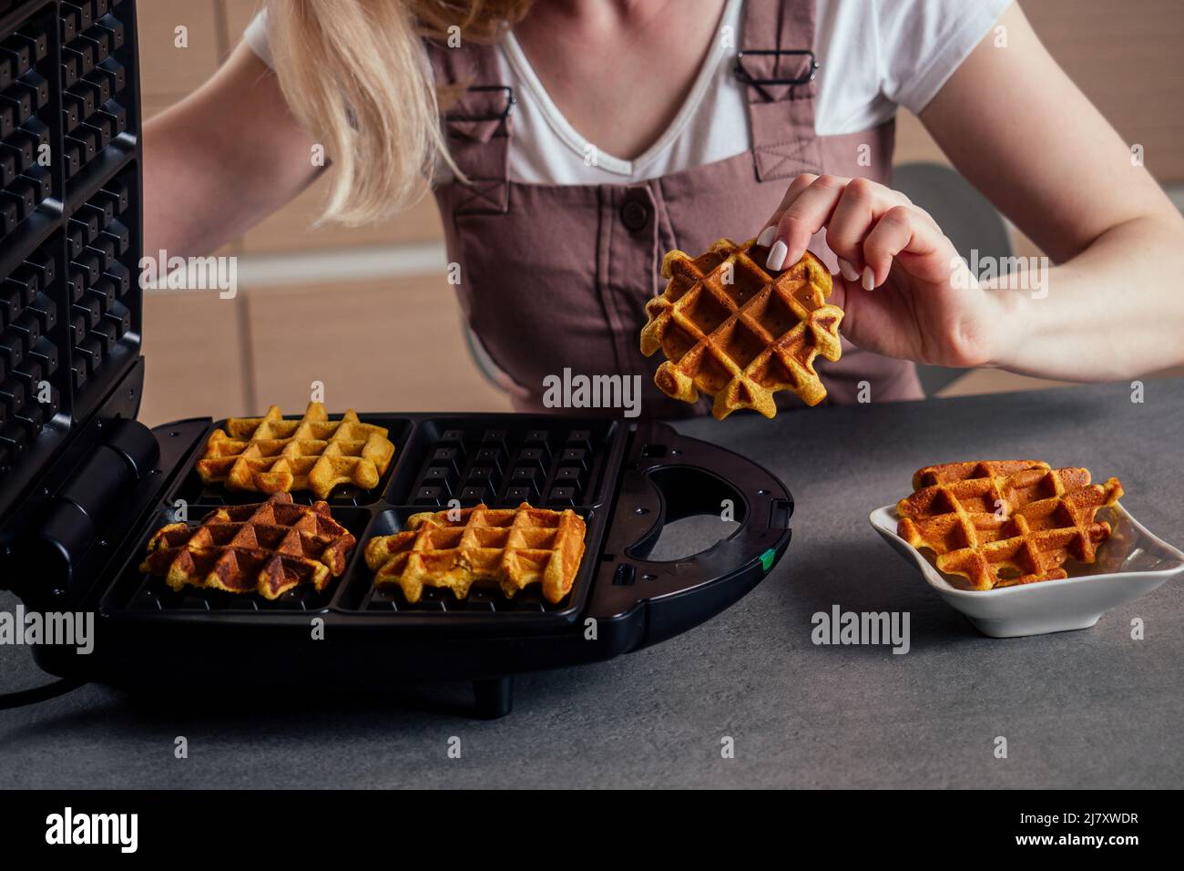 Woman taking fresh wafers out of waffle iron in kitchen Belgian waffles ...