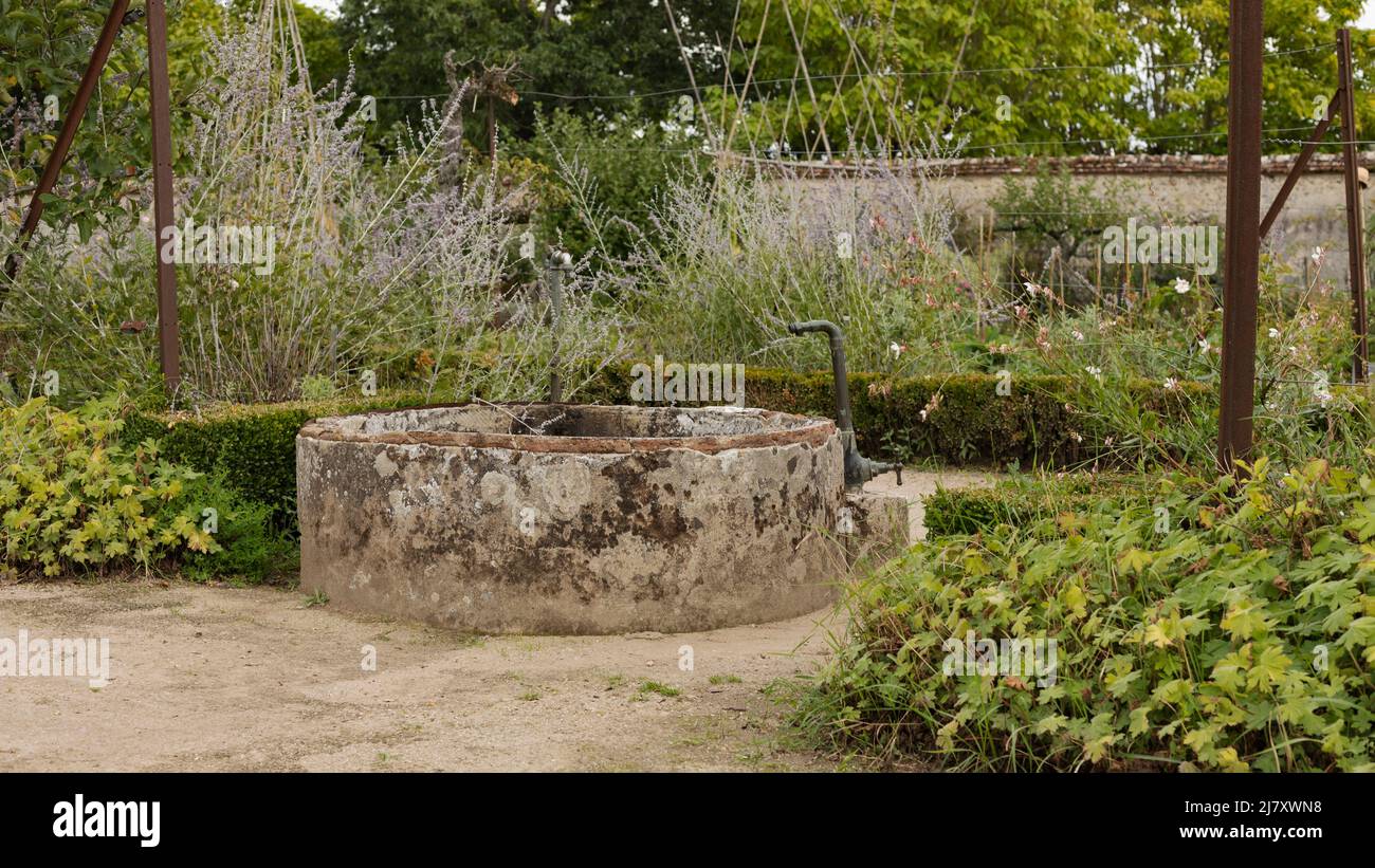 Old round stone well with a pipe where water comes out in a vegetable ...