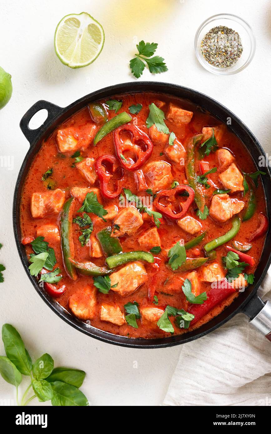 Thai style red chicken curry with vegetables in pan over white stone ...