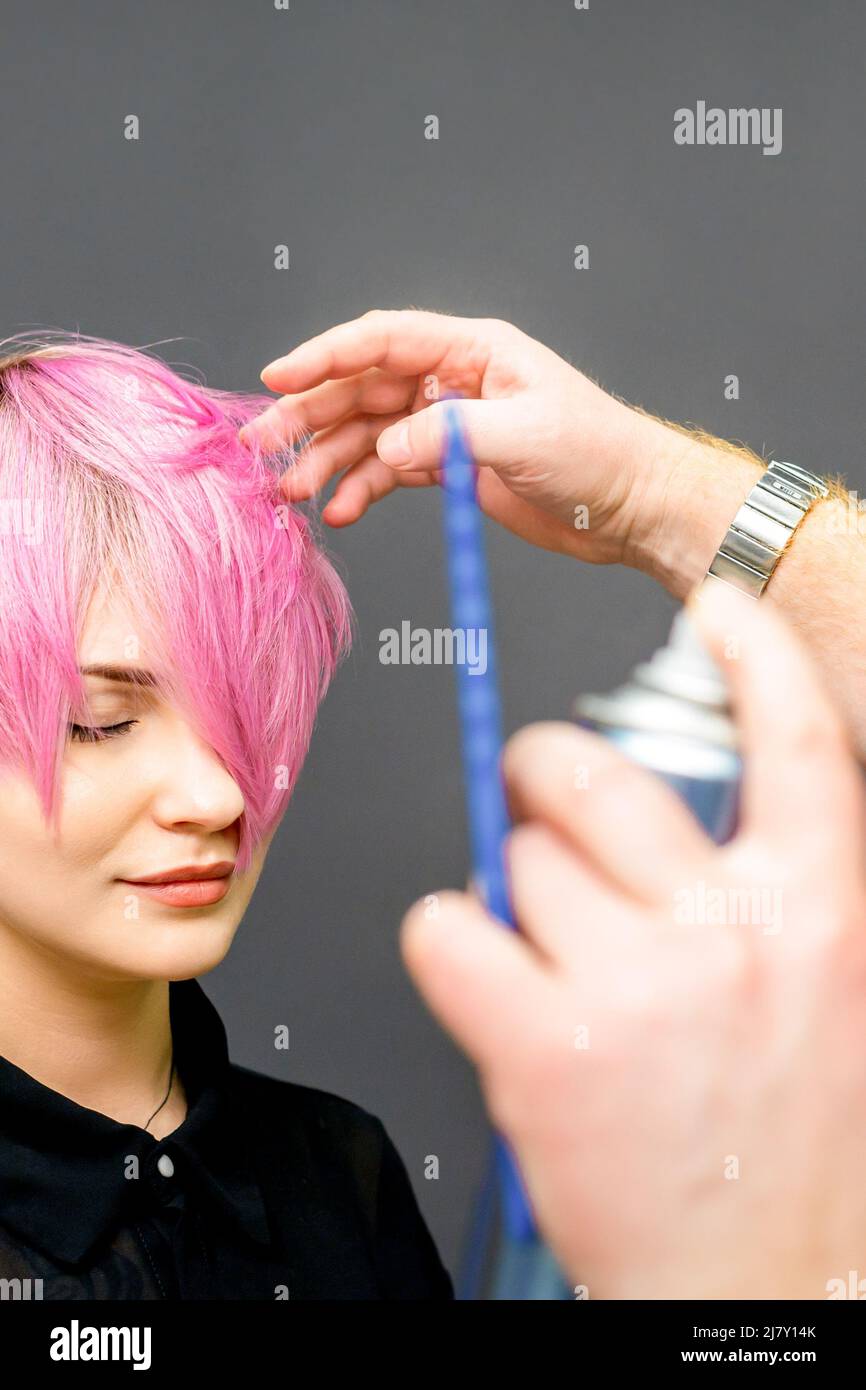 The hairdresser is using hair spray to fix the short pink hairstyle of ...