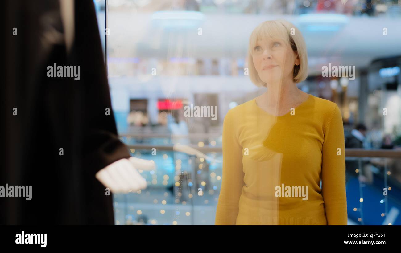 Mature middle aged caucasian woman looking sadly at showcase window ...