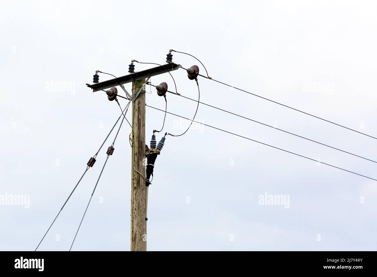Electricity cables fixed to a wooden poll with a blue sky background ...
