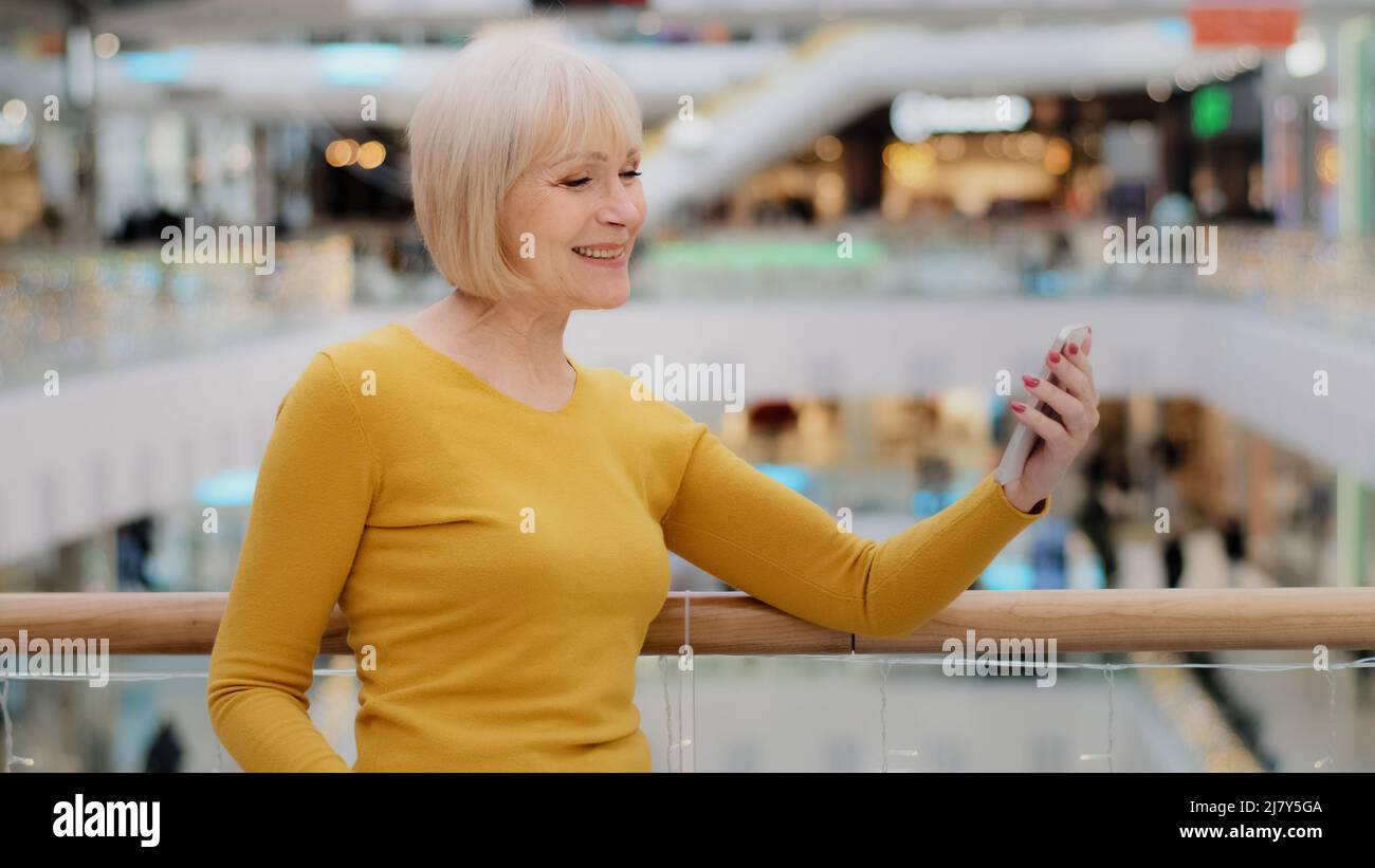 Happy mature middle aged woman holding smartphone in hand talking on video call using mobile app ...