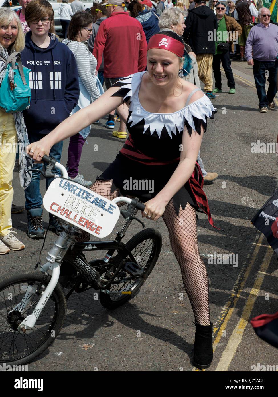 Young woman trying to ride an unrideable bike at the Brixham Pirate ...