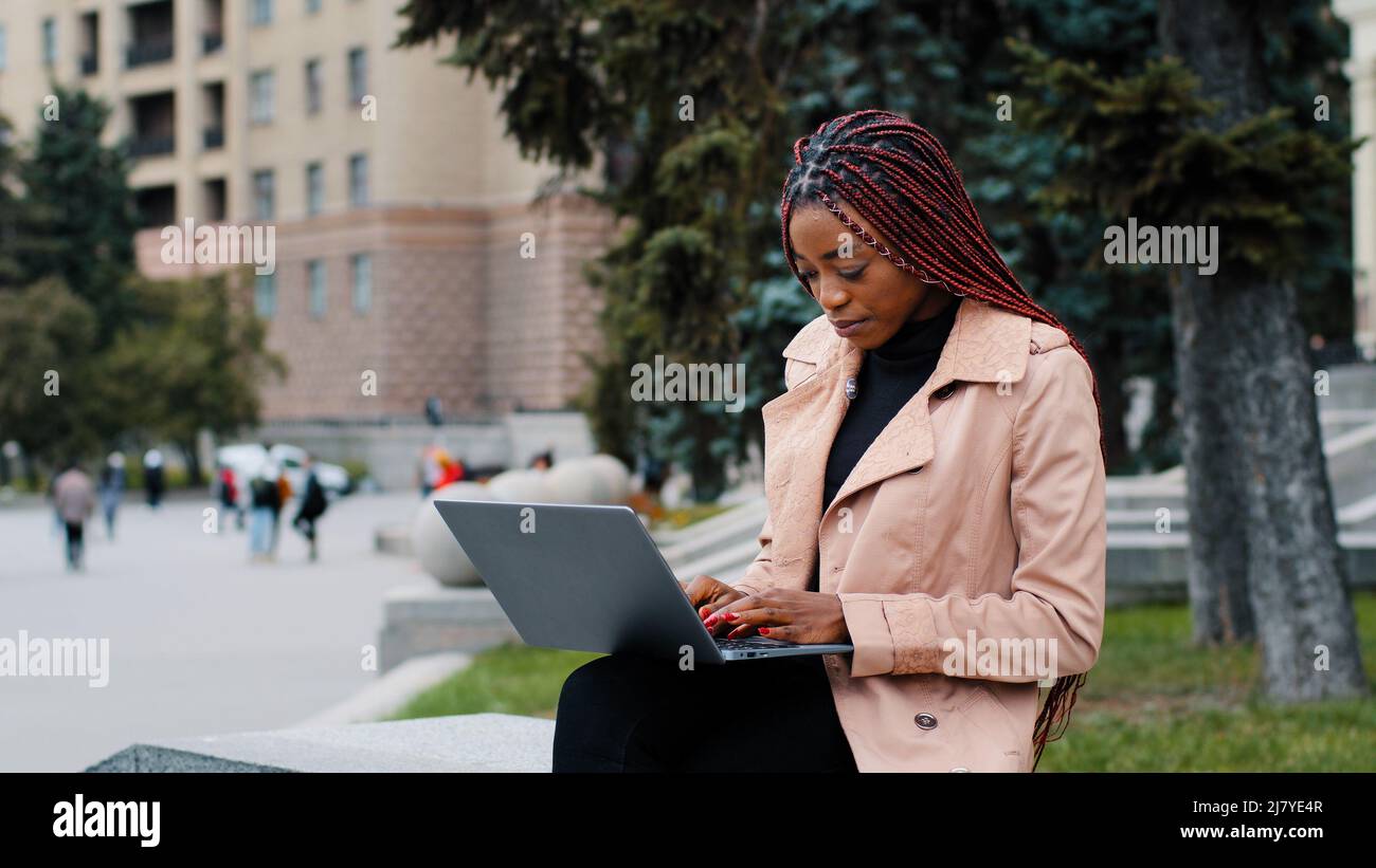 Serious african american girl blogger using laptop, sitting outdoor ...