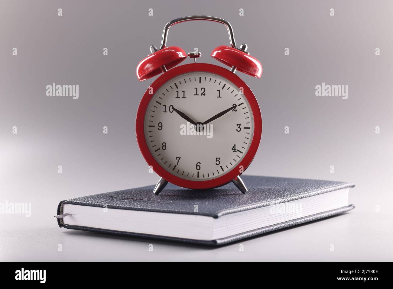 Red retro clock stand on top of closed book or diary, time to study ...