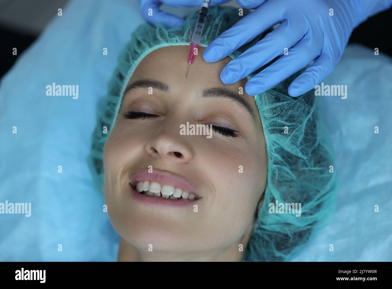 Smiling lady gets injection of botox in her forehead, cosmetologist ...