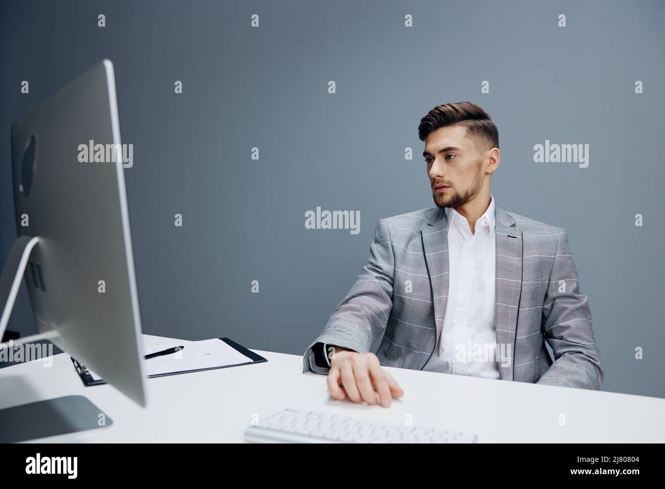 handsome man in a gray suit sits in front of a computer Gray background ...
