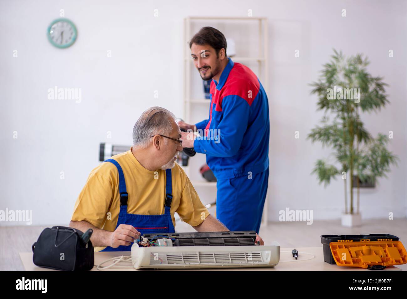 Two repairmen repairing air-conditioner at workshop Stock Photo - Alamy