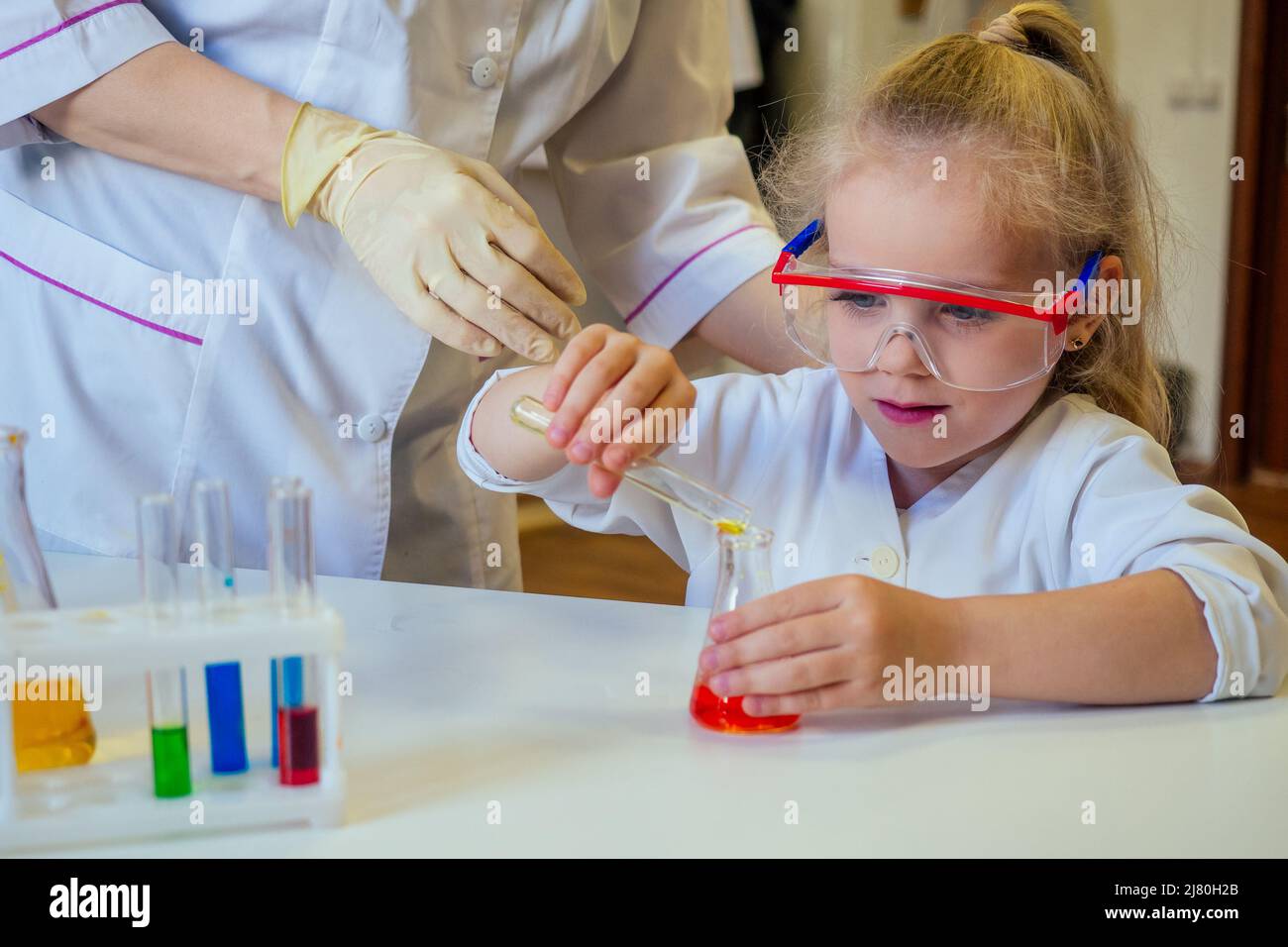 clever blonde school girl chemist in eyeglasses and white medical gown ...