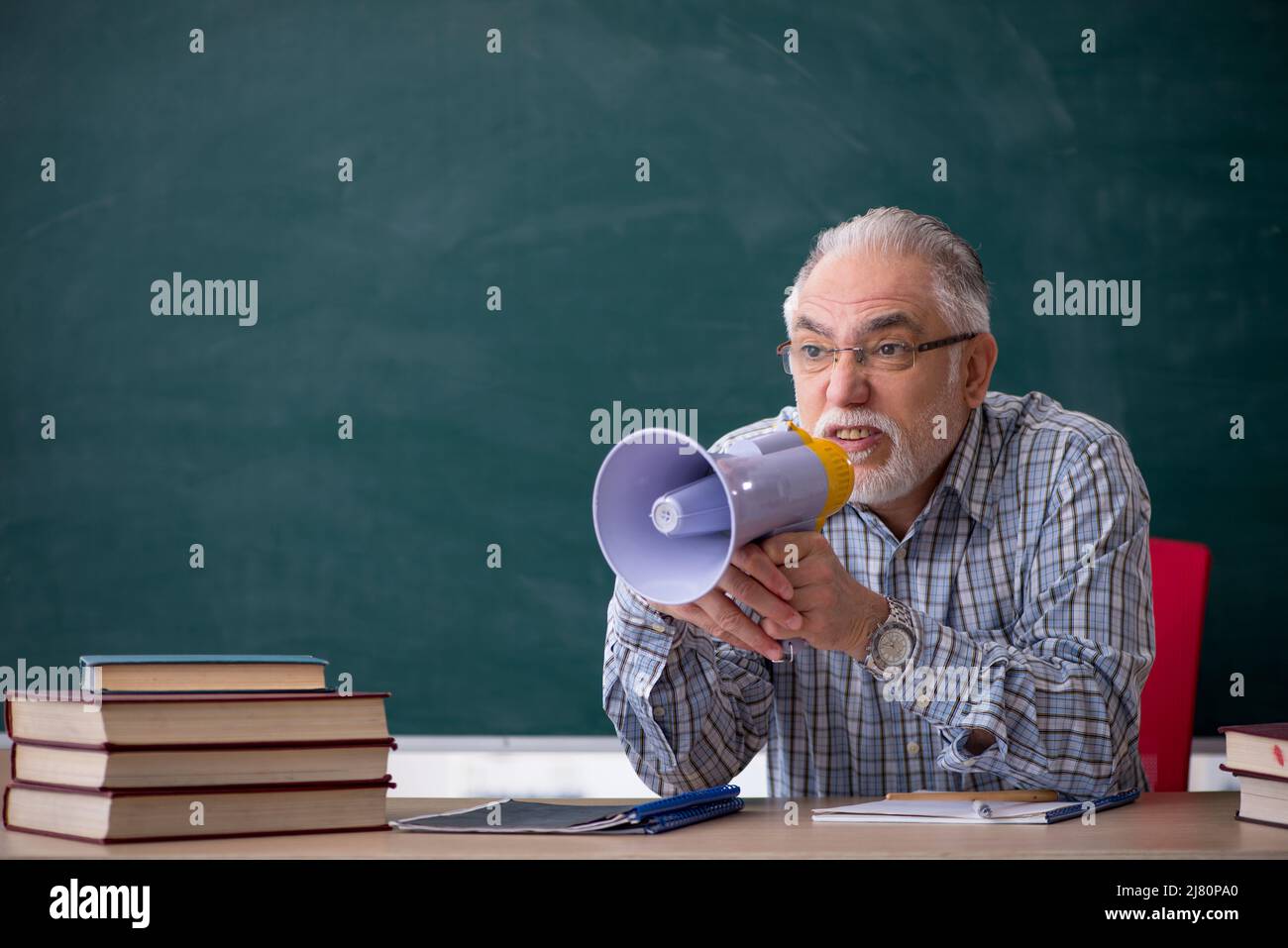 Aged male teacher holding megaphone in the classroom Stock Photo - Alamy