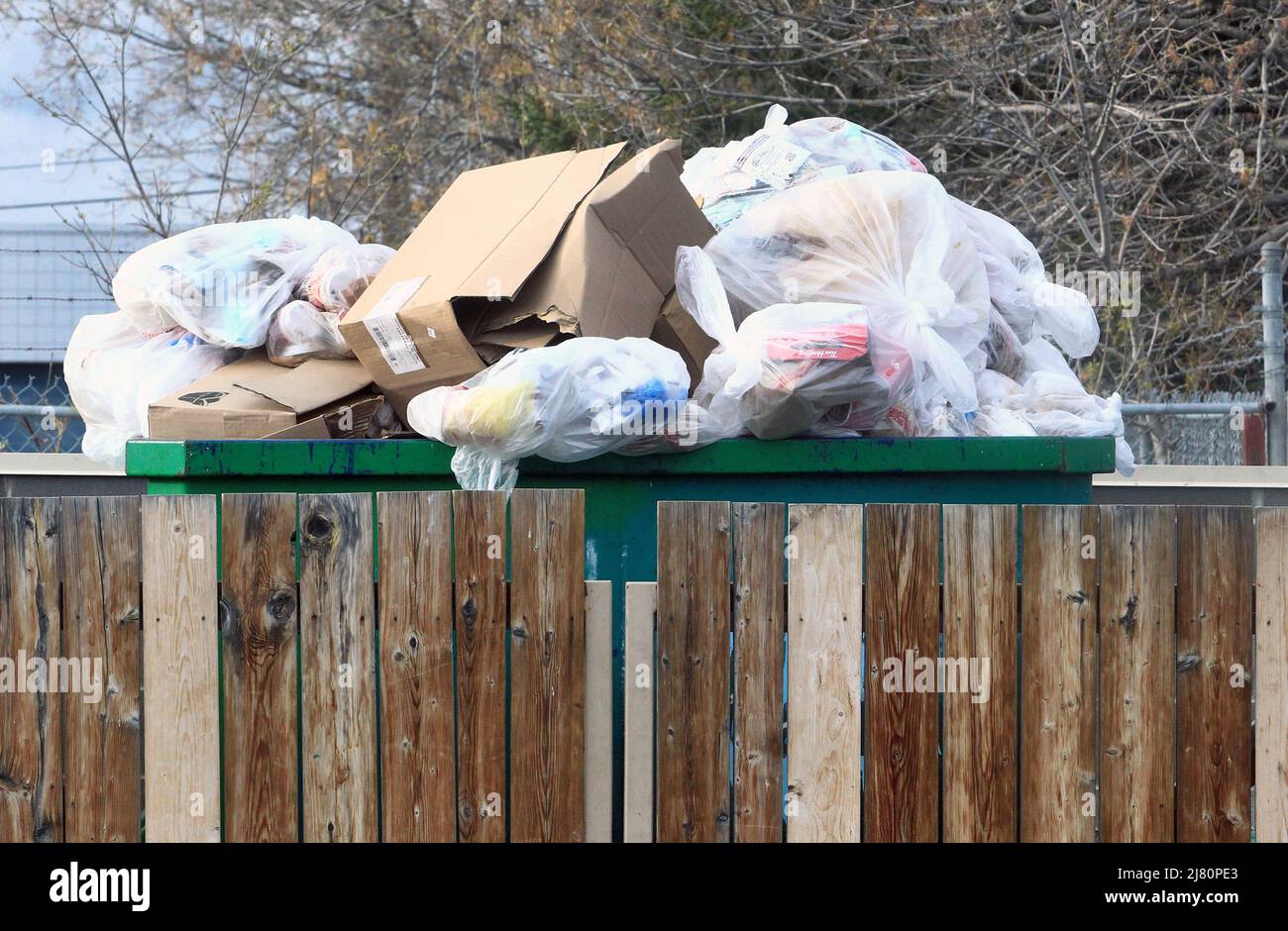 Outdoor large garbage dumpster overflowing with trash inside a wooden ...