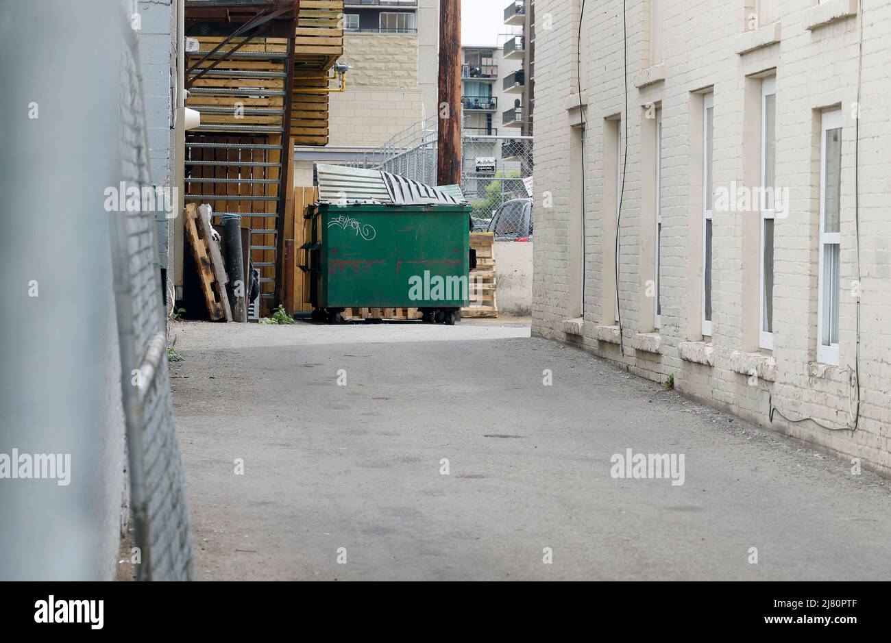 Empty back alleyway in a city in the daytime with a large garbage ...