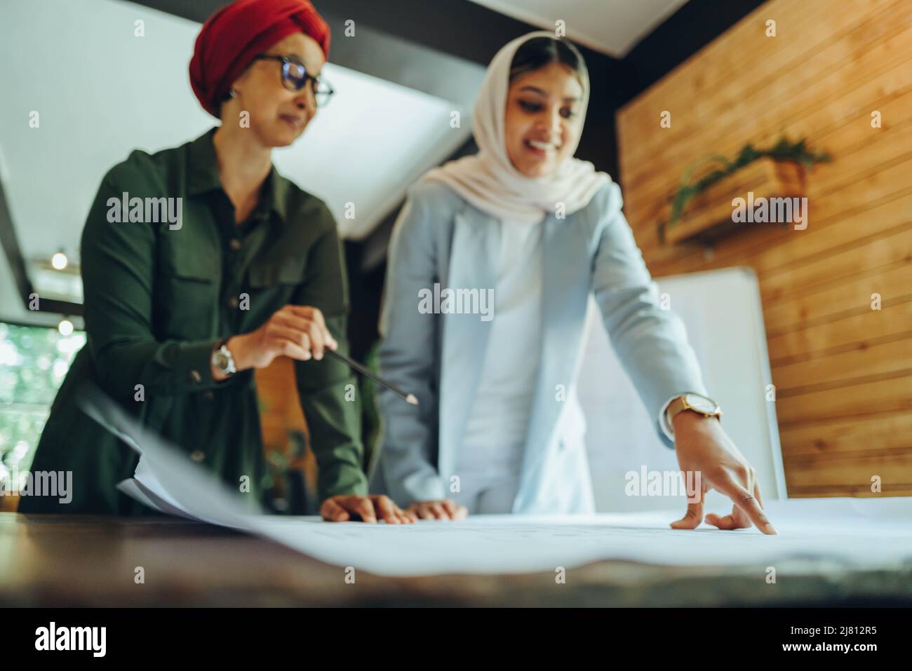 Female architects working on blueprint drawings in a modern office. Two Muslim businesswomen ...