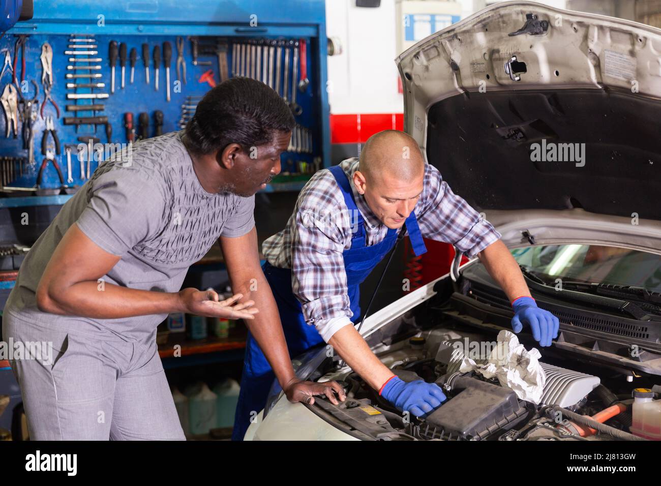 Worried client talking with specialist about repairing his car engine ...