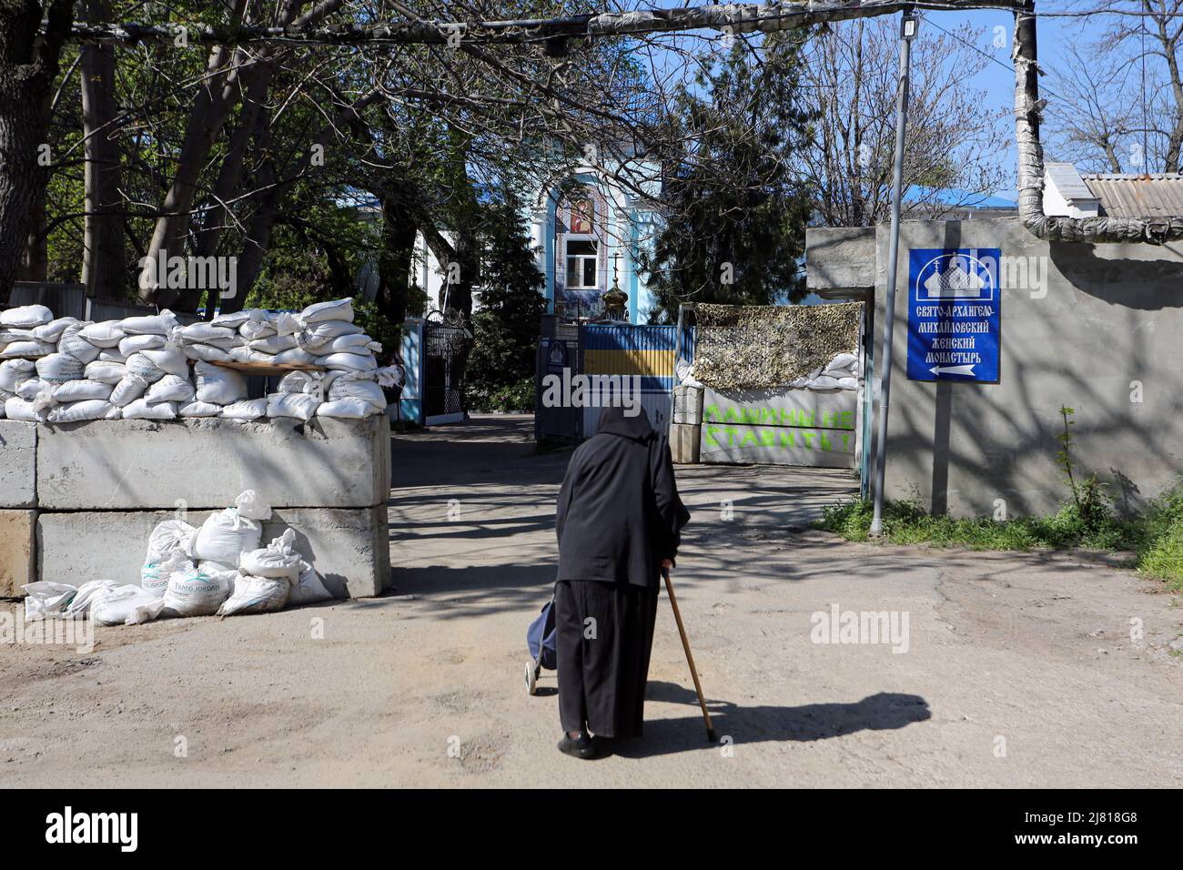 An elderly nun in a black cassock with a stick and a wheelbarrow in her ...
