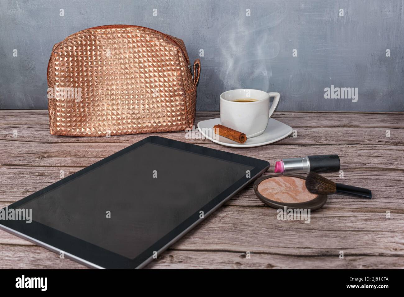 Tablet on the table surrounded by lipstick, pressed powder, coffee cup ...