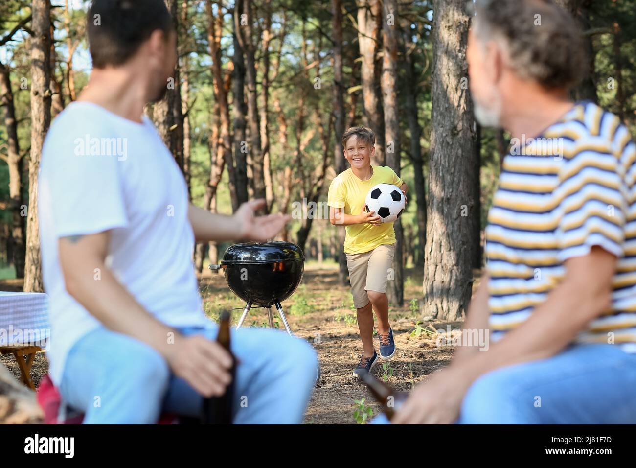 Little boy with ball running to his father and grandfather in forest ...