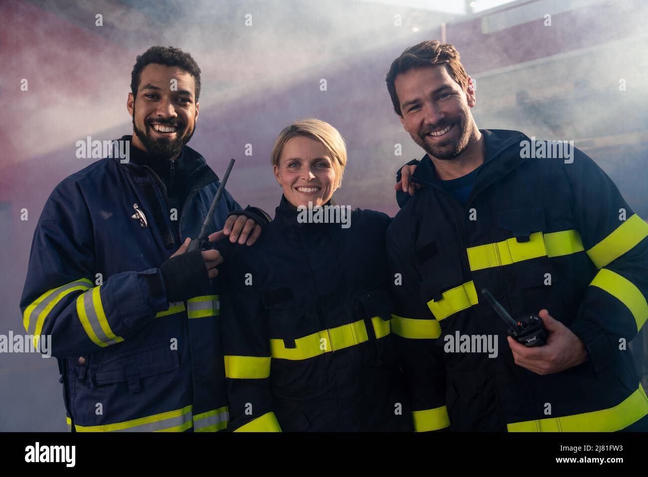 Happy firefighters crew with fire station and truck in background ...