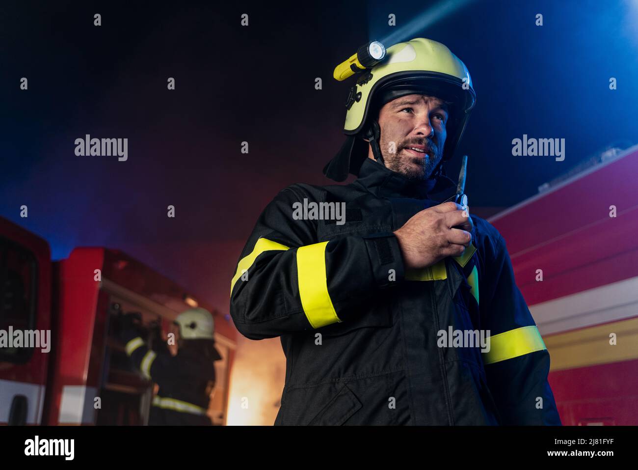 Low angle view of firefighter with fire truck in background at night ...