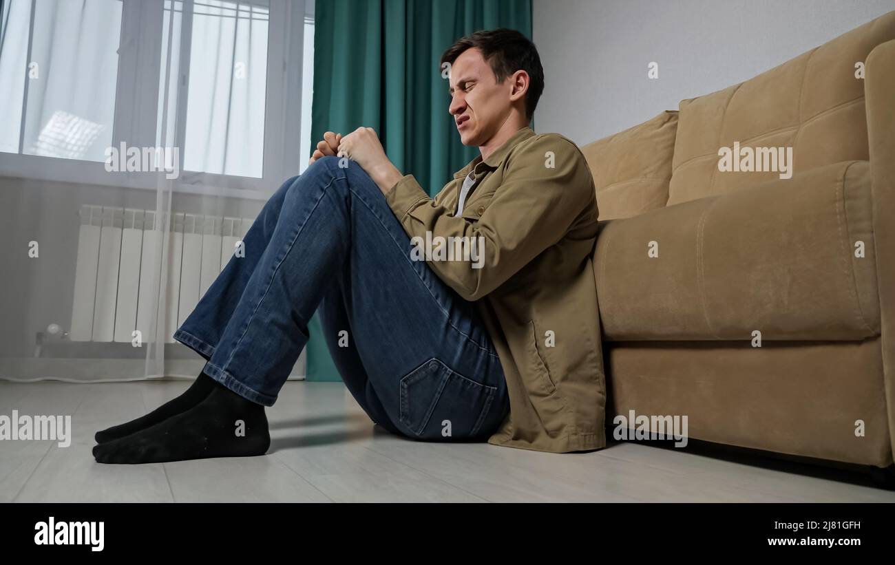 sad upset man sits on floor near sofa in living room Stock Photo - Alamy
